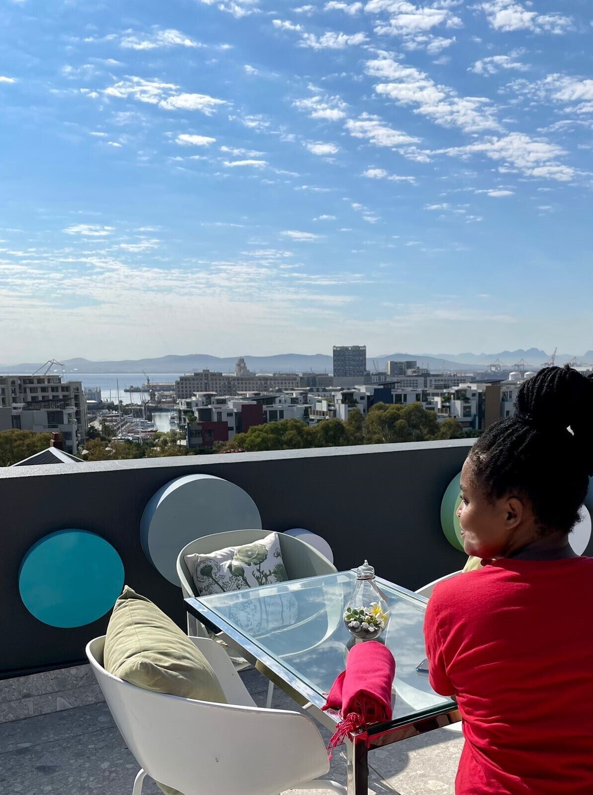 Criança numa varanda com vista para um horizonte urbano, incluindo edifícios e um corpo de água.
