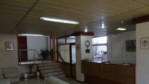 Uma área de recepção com balcão de madeira, um sofá, uma escada e um vaso de planta.