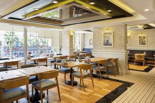 Um restaurante moderno com mesas e cadeiras de madeira, grandes janelas e uma parede de destaque em tijolo.