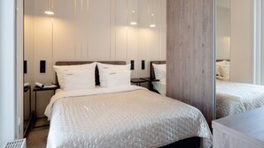 Quarto de hotel com uma cama grande, mesas de cabeceira e um espelho.
