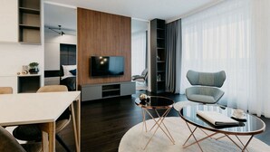 Uma sala de estar moderna com televisão de tela plana, uma mesa de centro redonda e um espaço de estar confortável.