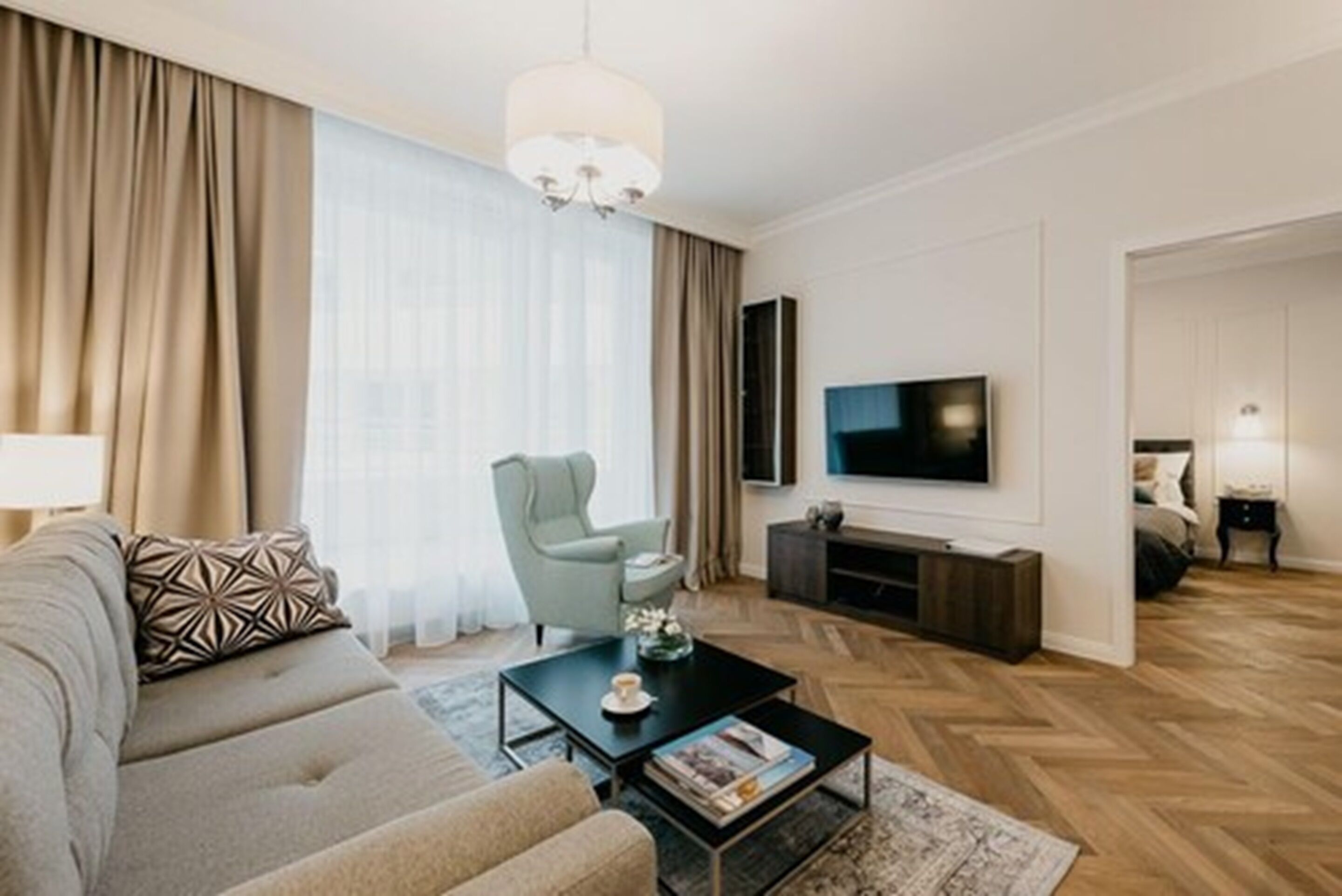 Uma sala de estar moderna com sofá, poltrona, mesa de centro, TV e lustre.