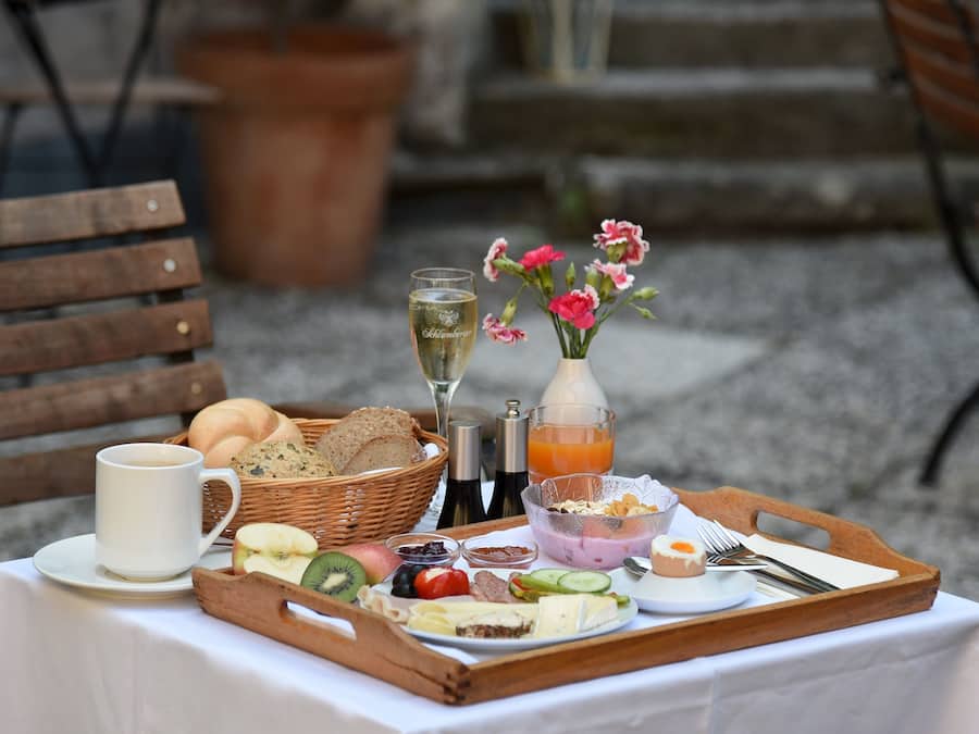 Uma bandeja de café da manhã com pão, frutas, queijo e bebidas em uma mesa ao ar livre.