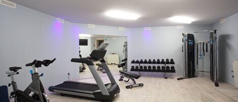 Uma academia com equipamentos de ginástica, incluindo esteira, bicicleta ergométrica e halteres.