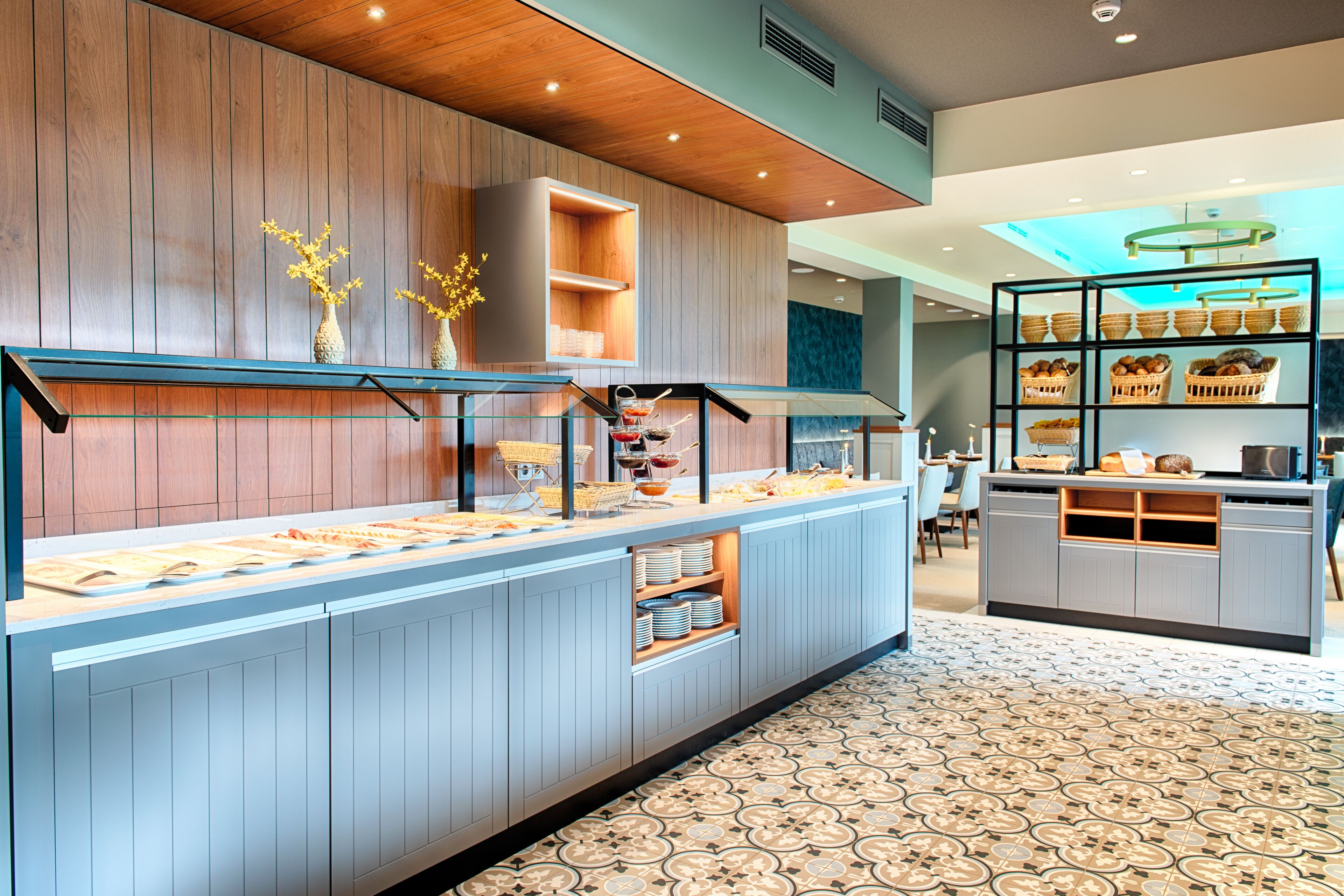 Espaço de buffet com parede de painel de madeira, piso ladrilhado e uma variedade de produtos de panificação.