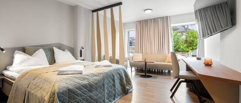Quarto de hotel moderno com cama, escrivaninha, cadeira e televisão.