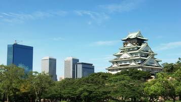 Um castelo japonês tradicional cercado por arranha-céus modernos e um parque verde.