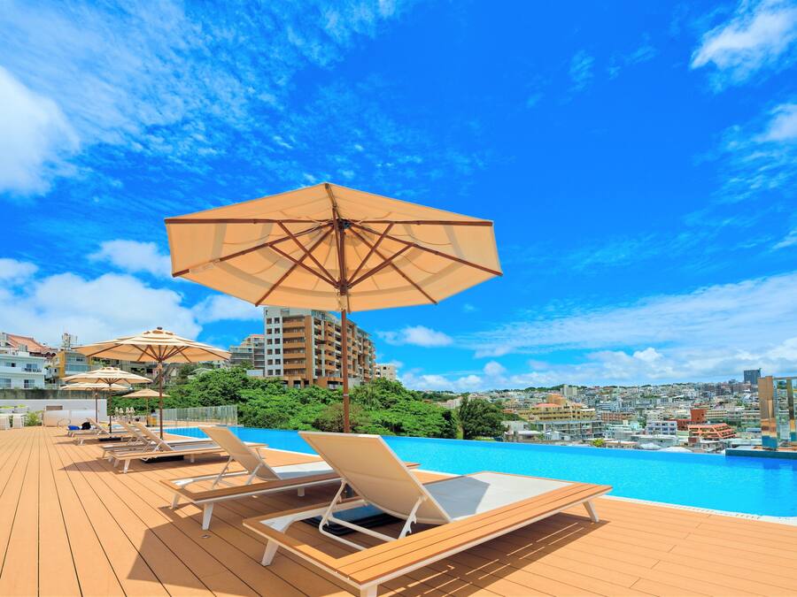 Uma área de piscina no terraço com espreguiçadeiras e guarda-sóis, com vista para a paisagem urbana.