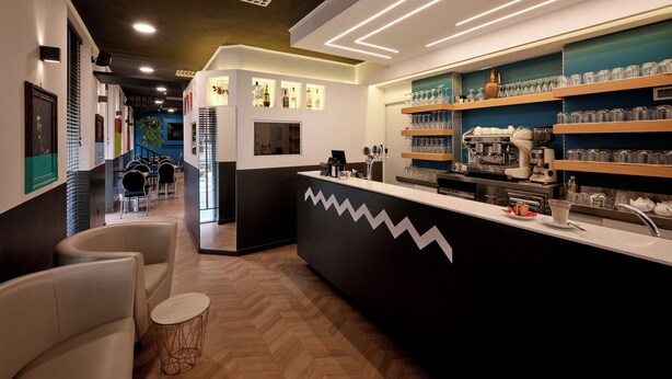 Uma área de bar moderna com balcão, assentos e prateleiras com copos e garrafas.