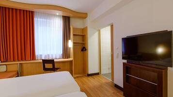Quarto de hotel com cama, escrivaninha, televisão e guarda-roupa.