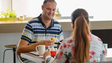 Um homem e uma mulher sentados à mesa, com uma xícara e um prato de comida.