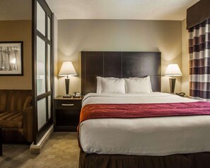 Quarto de hotel com uma cama grande, duas mesas de cabeceira com luminárias, uma cadeira e uma janela com persianas.