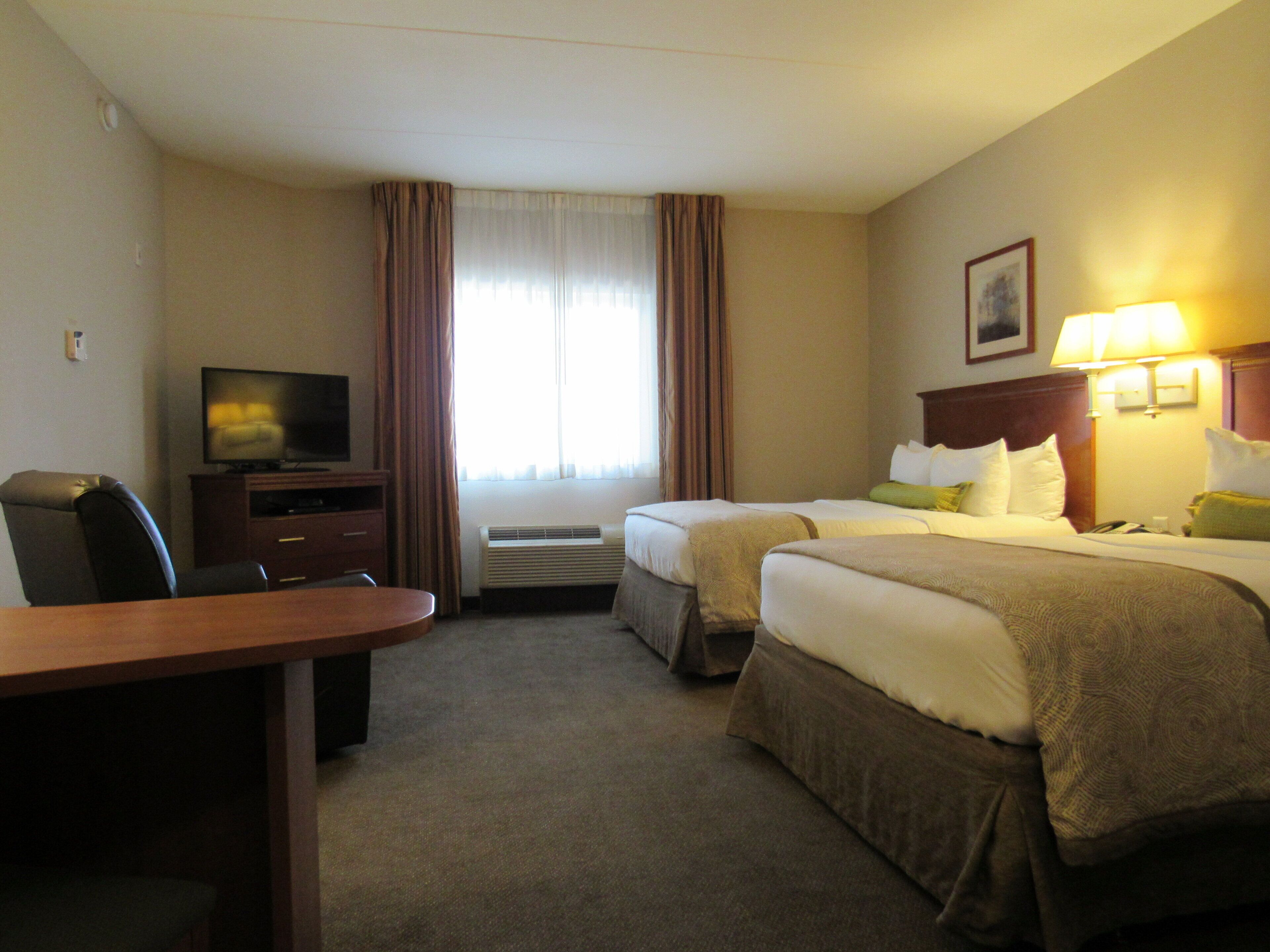 Quarto de hotel com duas camas, uma escrivaninha, televisão e ar condicionado.