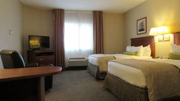 Quarto de hotel com duas camas, uma escrivaninha, televisão e ar condicionado.