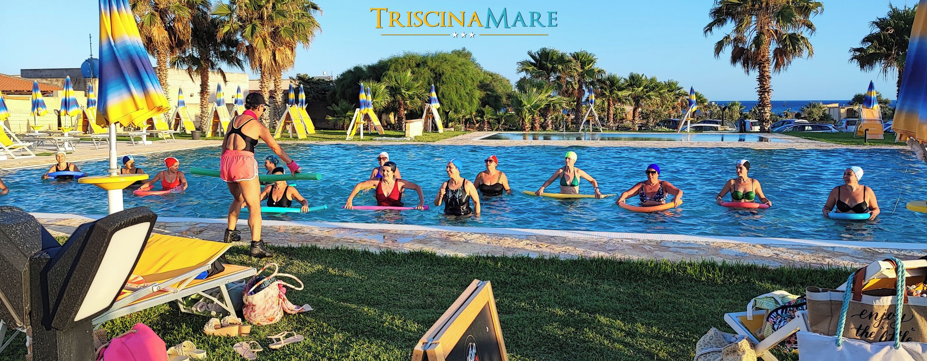 Uma área de piscina com pessoas na água, espreguiçadeiras e guarda-sóis.