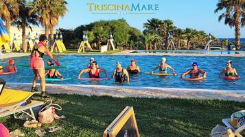 Uma área de piscina com pessoas na água, espreguiçadeiras e guarda-sóis.