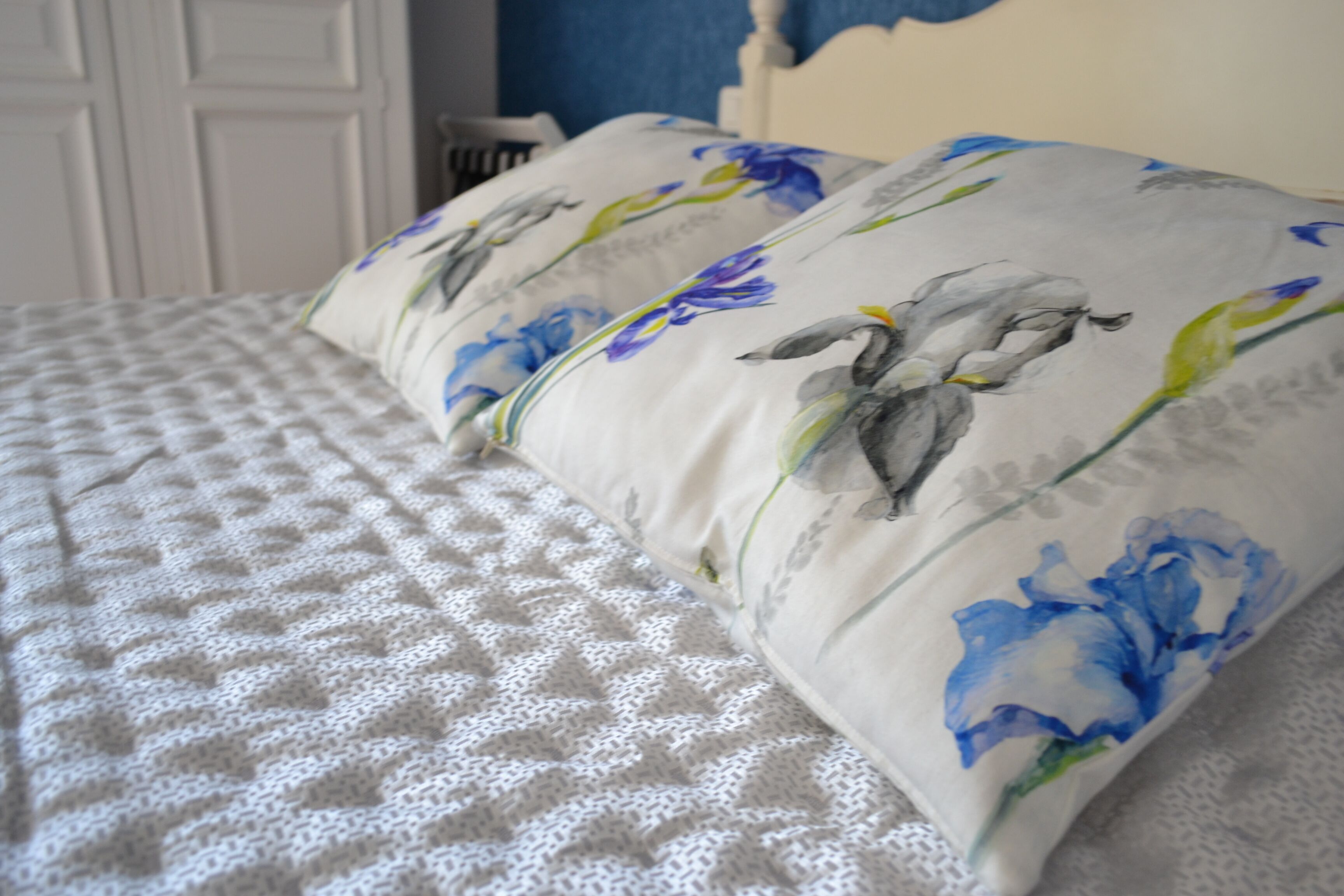 Uma cama com cobertura acolchoada branca e dois travesseiros estampados com flores.