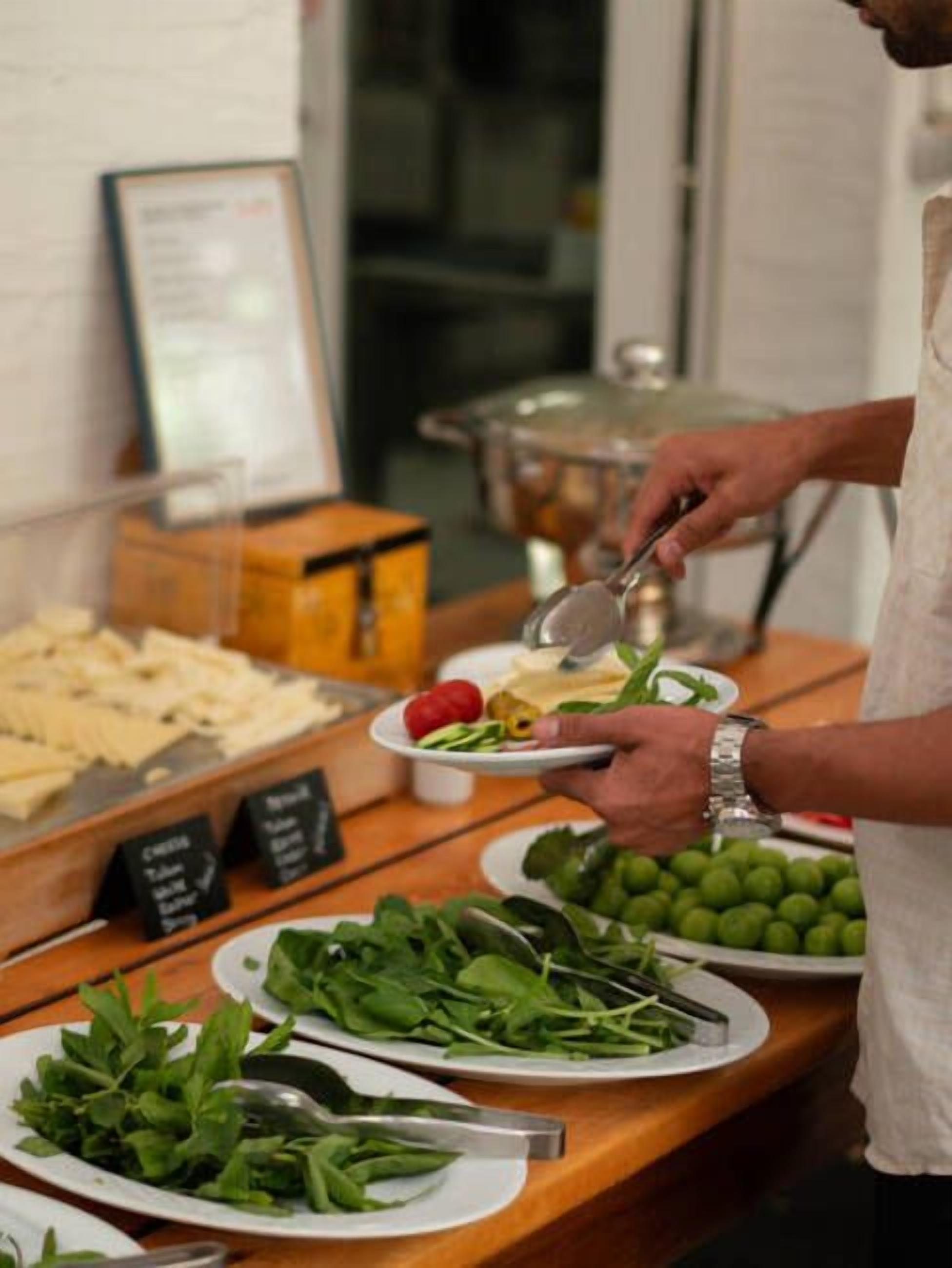 Uma pessoa preparando comida em um buffet com diversos pratos e ingredientes à mostra.