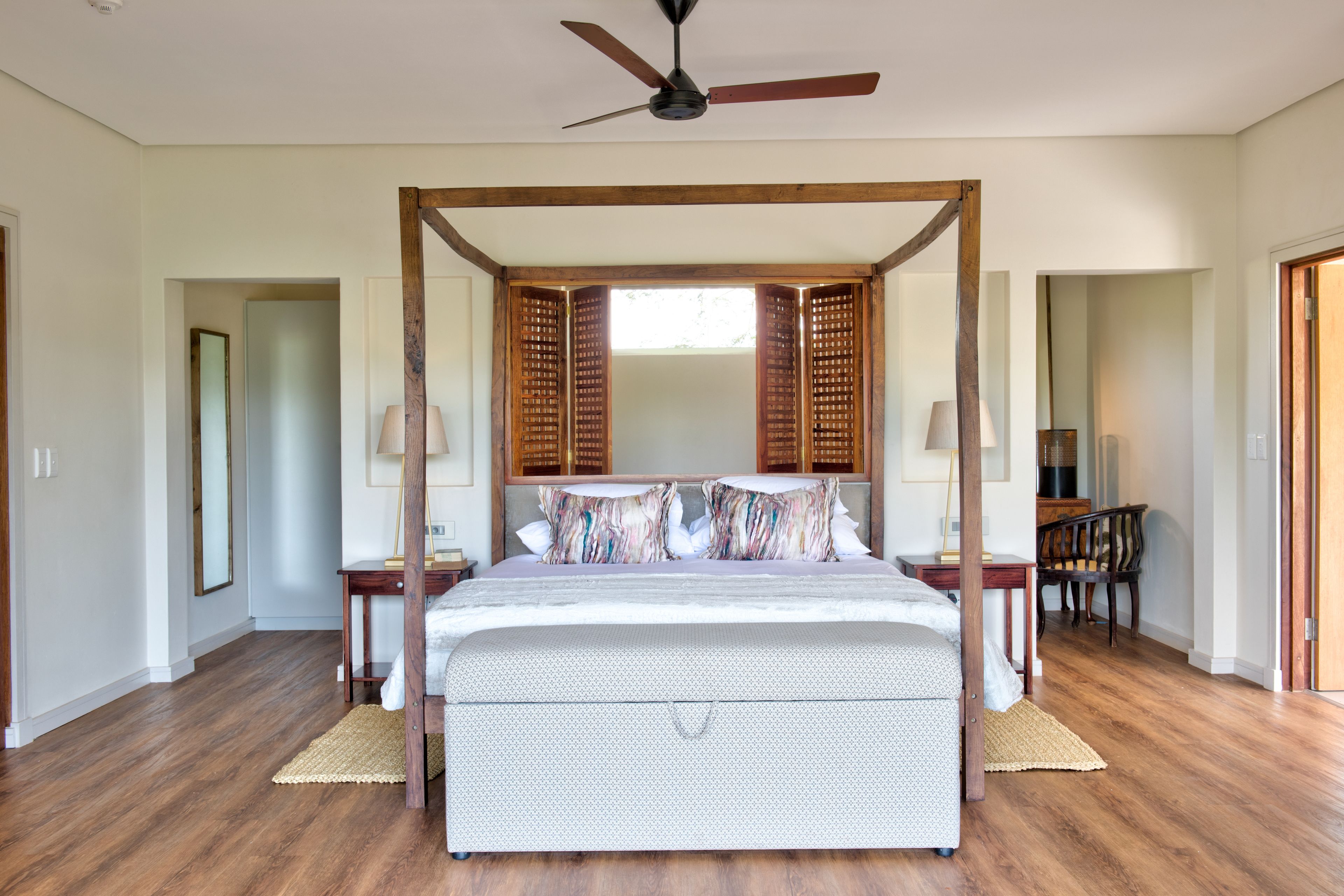 Uma cama de dossel com estrutura de madeira, um ventilador de teto e uma mesa de cabeceira com abajur.
