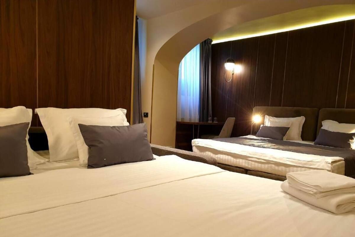 Quarto de hotel com duas camas, uma parede curva e uma mesa de cabeceira com abajur.