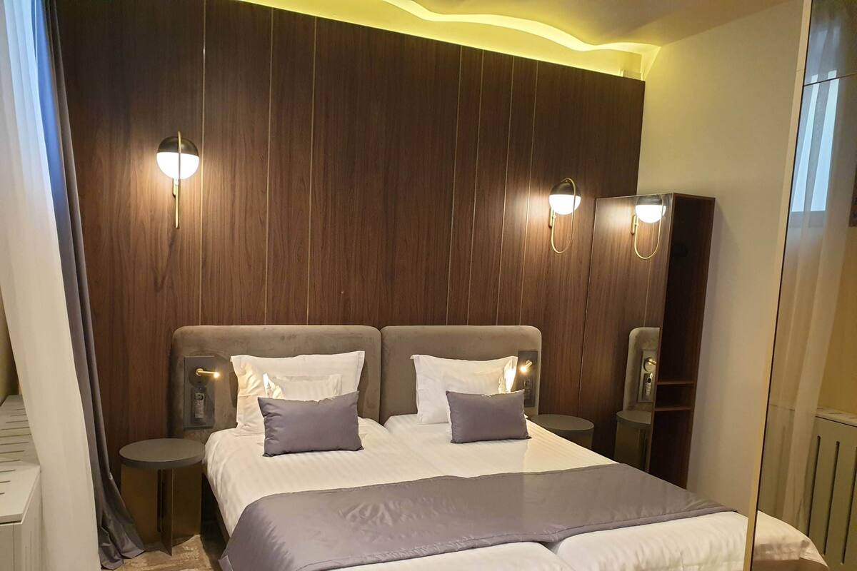 Quarto com cama grande, duas mesas de cabeceira, espelho e parede de painéis de madeira.