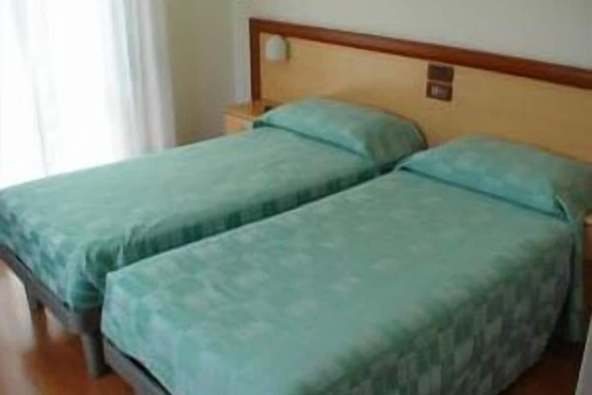 Quarto com duas camas de solteiro, cabeceiras de madeira e mesa de cabeceira com abajur.