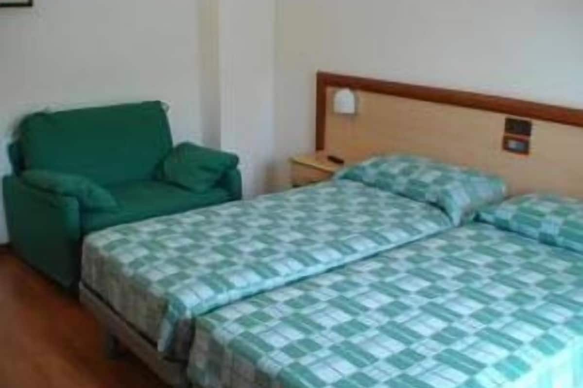 Um quarto com uma cama, uma poltrona verde e uma mesa de cabeceira com abajur.