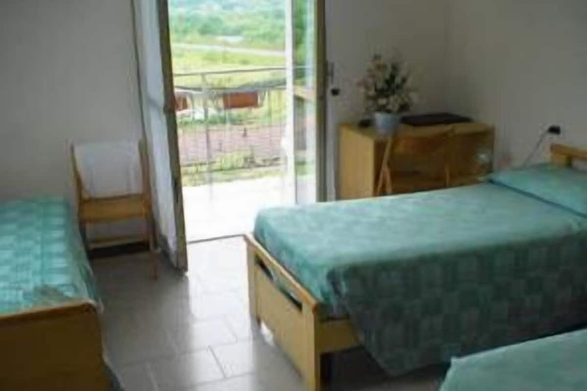 Quarto com duas camas, uma escrivaninha e uma cadeira.