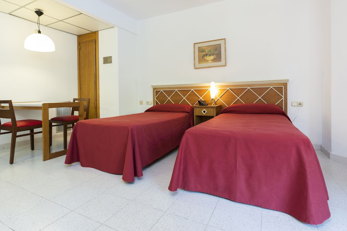 Quarto de hotel com duas camas, uma mesa e uma cadeira.