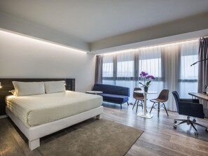 Quarto de hotel moderno com uma cama grande, um sofá, uma escrivaninha e uma pequena mesa com cadeiras.