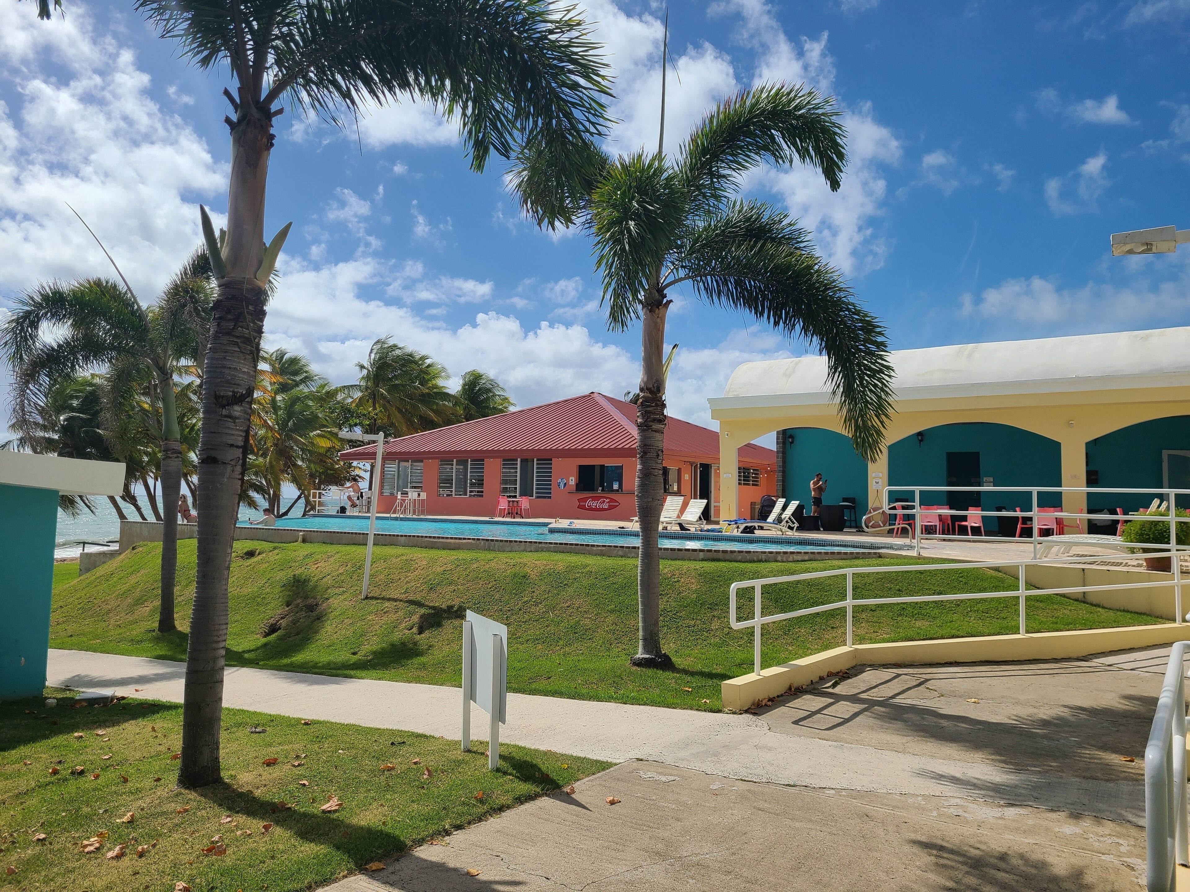 Área da piscina com espreguiçadeiras e um edifício com telhado vermelho.