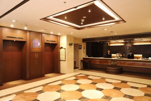 Um saguão de hotel com balcão de recepção, elevadores e piso estampado.