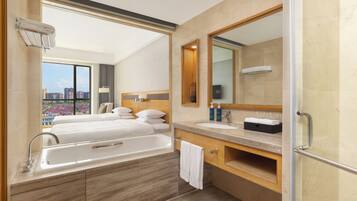 Quarto de hotel com uma cama grande, uma banheira, uma toucador com espelho e vista para a cidade pela janela.