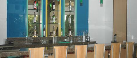 Uma área de bar com diversas opções de assento, um balcão com utensílios de bar e prateleiras cheias de garrafas e copos.