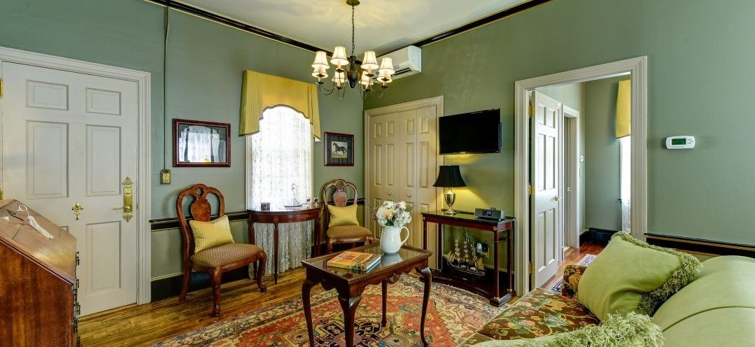 Uma sala de estar tradicional com piso de madeira, um candelabro, uma televisão e um sofá verde.