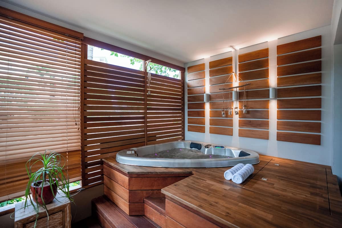 Um banheiro moderno com uma banheira de madeira, uma pequena mesa com um vaso de planta e um porta-toalhas.