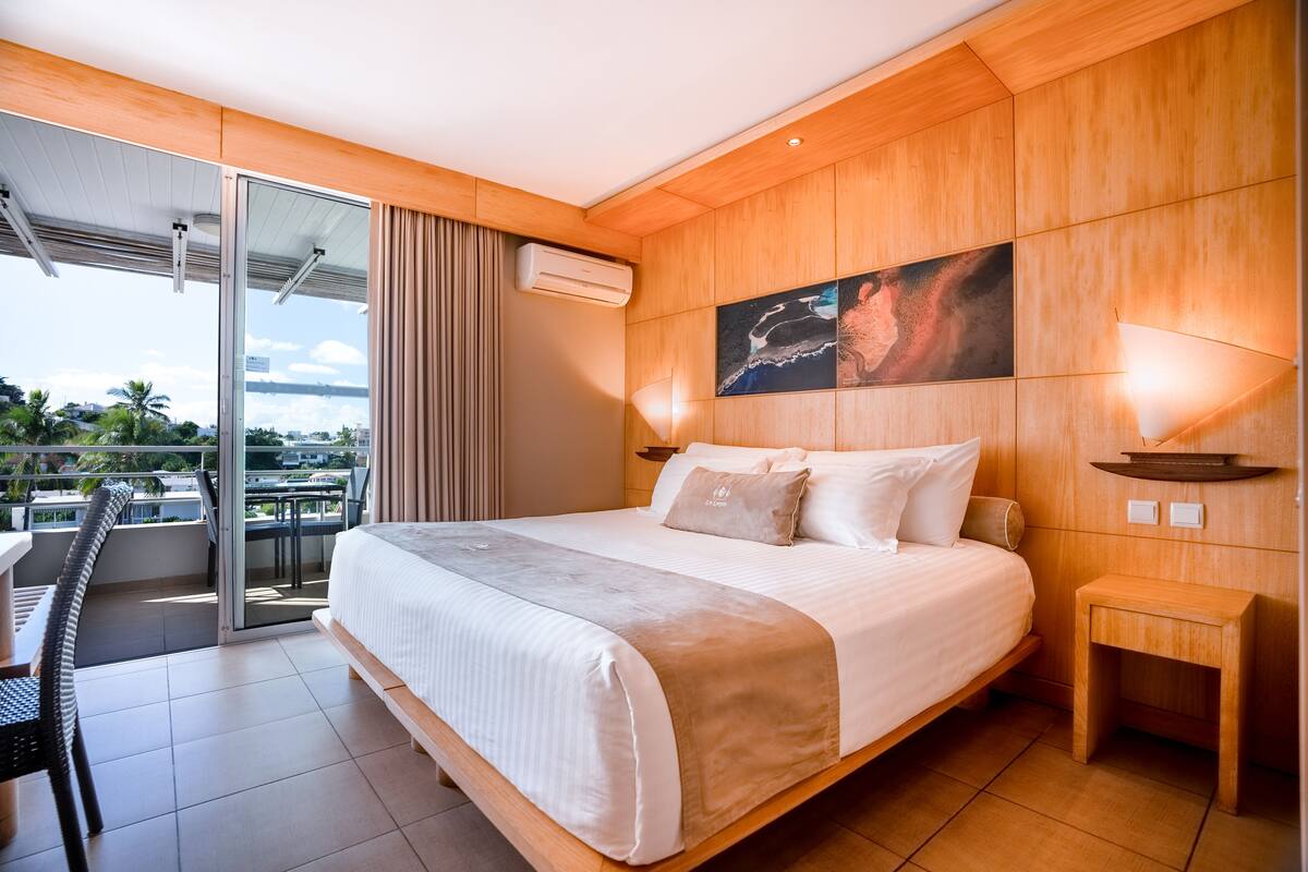 Quarto de hotel moderno com uma cama grande, varanda com vista e painéis de madeira.