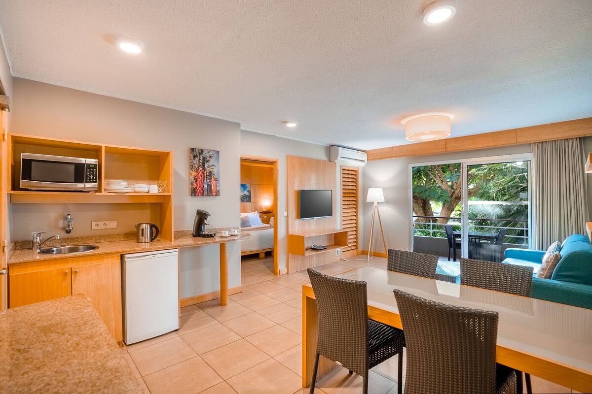 Quarto de hotel compacto com cozinha compacta, área de refeições, televisão e janela com vista para área verde.