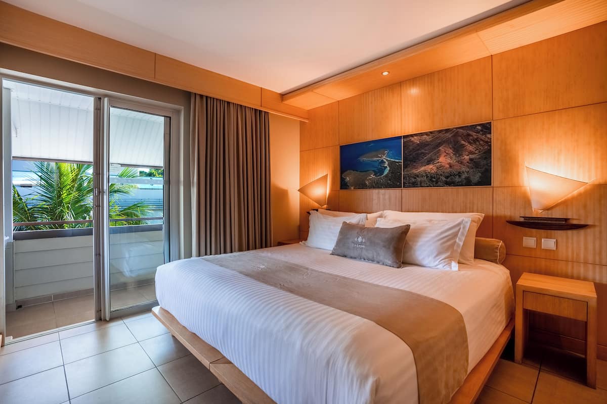 Quarto de hotel moderno com uma cama grande, porta de vidro deslizante para uma varanda e vista para o exterior.