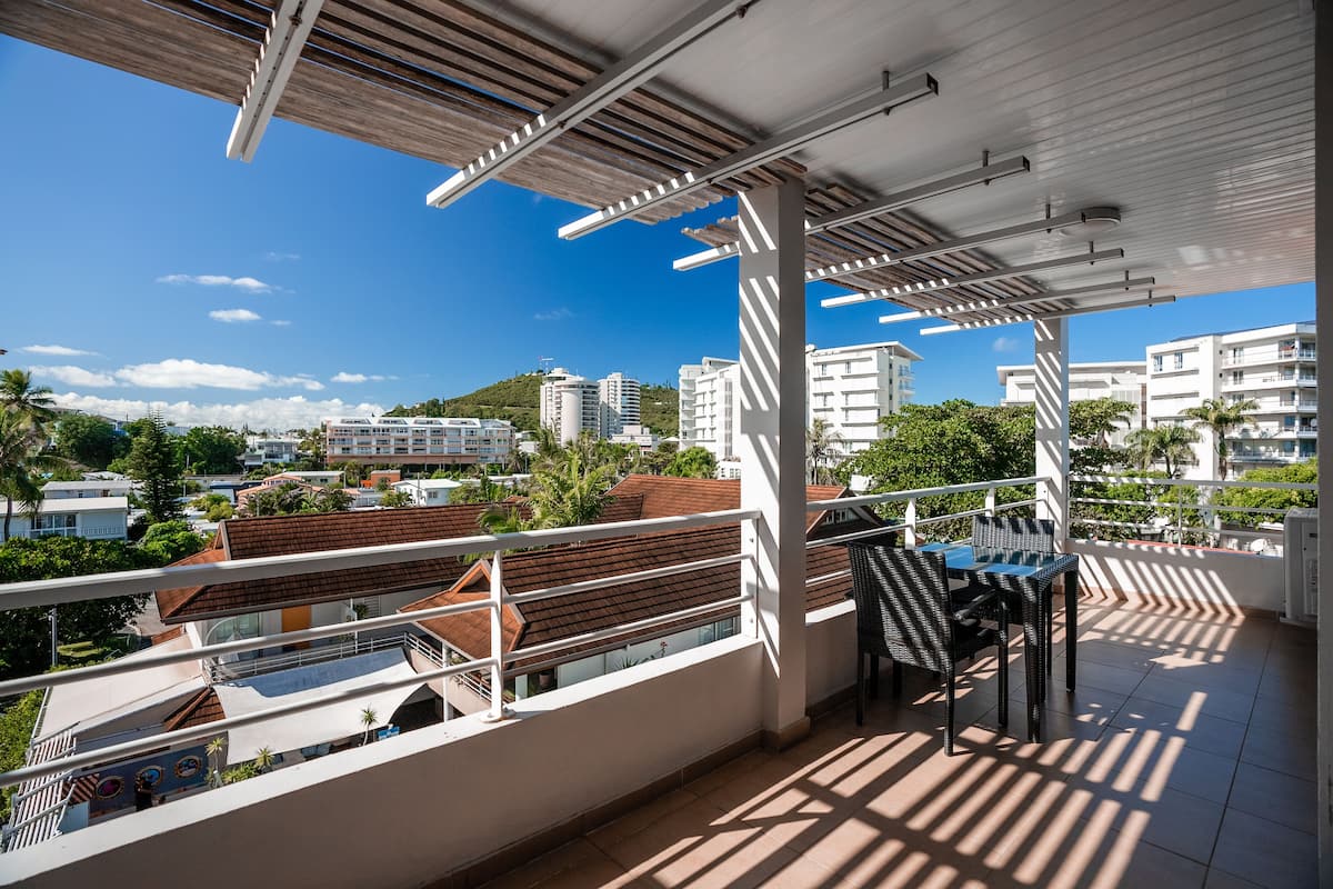 Varanda com mesa e cadeiras, vista para um horizonte urbano com edifícios e áreas verdes.