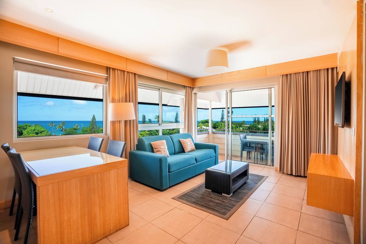 Quarto de hotel moderno com sofá, mesa de jantar e televisão.