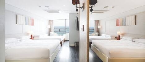 Quarto de hotel moderno com duas camas, um espelho grande e vista para o mar.