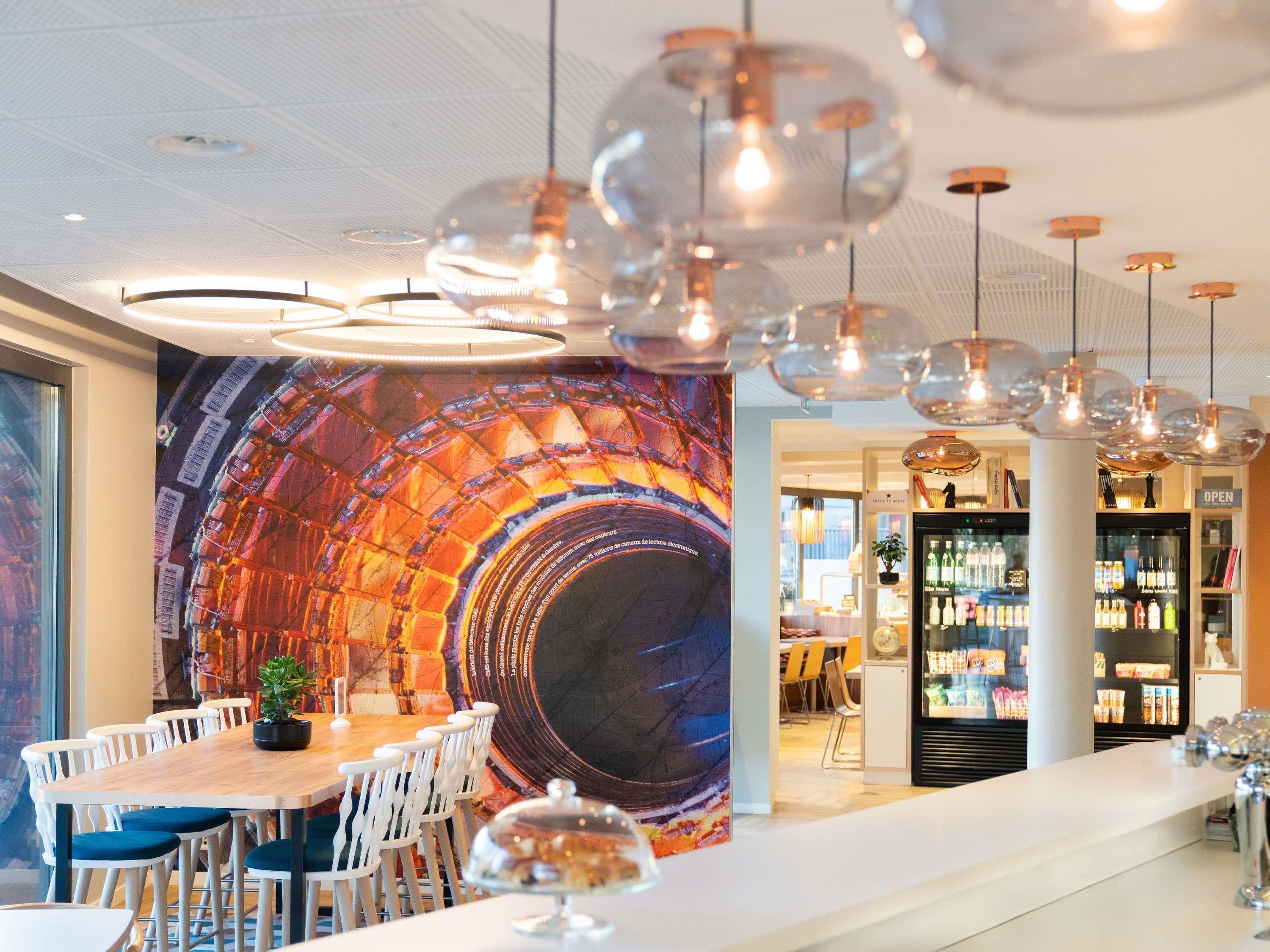 Um restaurante com um grande mural, luminárias pendentes e um espaço de bar.