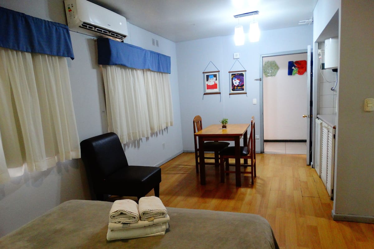 Quarto de hotel com cama, cadeira, mesa e uma pequena planta em vaso.