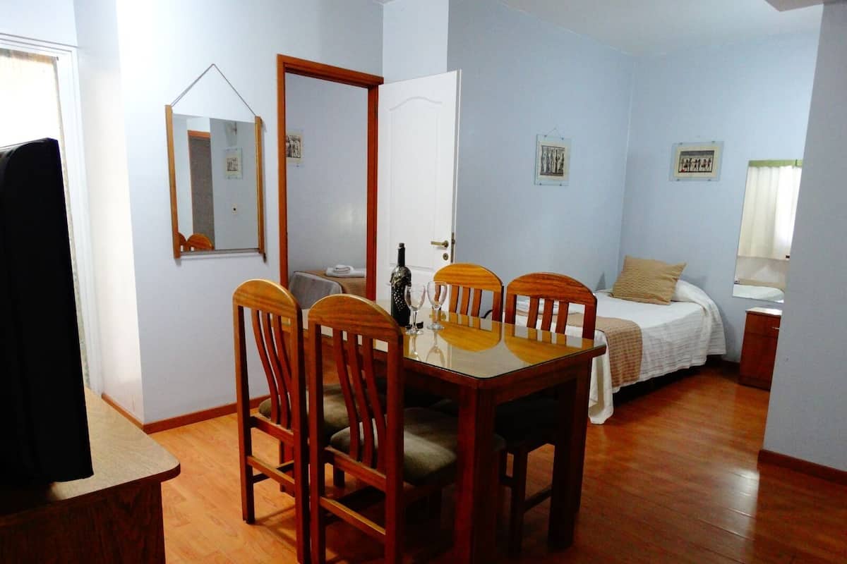 Quarto pequeno com mesa de jantar e cadeiras, uma cama, mesa de cabeceira e espelho na parede.