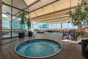 Área de piscina no terraço com hidromassagem, espreguiçadeiras e plantas em vasos.