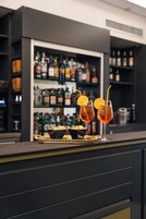 Uma área de bar com dois copos de uma bebida vermelha, decorados com fatias de laranja, e uma bandeja de petiscos.