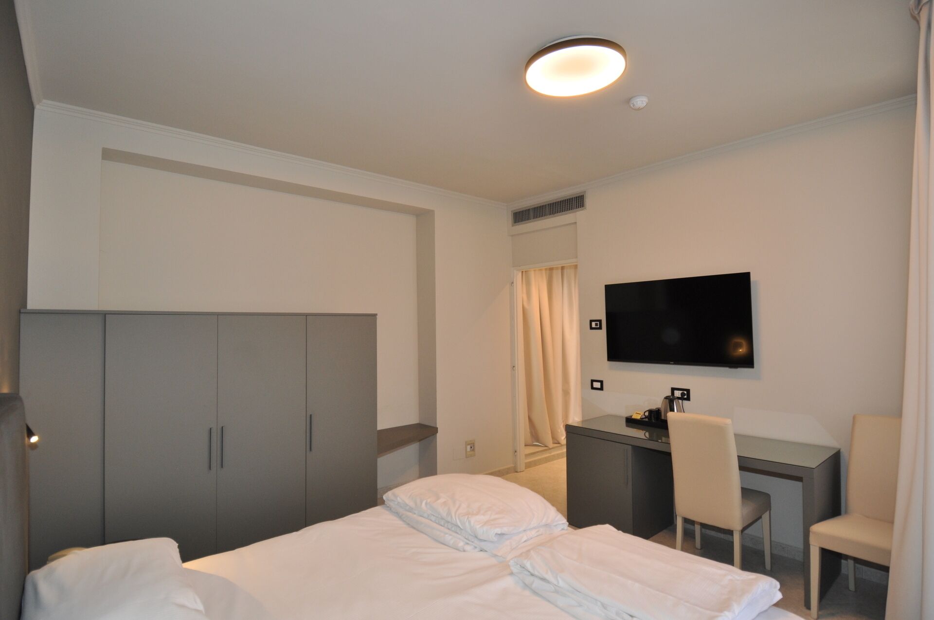 Quarto de hotel com cama, escrivaninha, cadeira, televisão e armário.