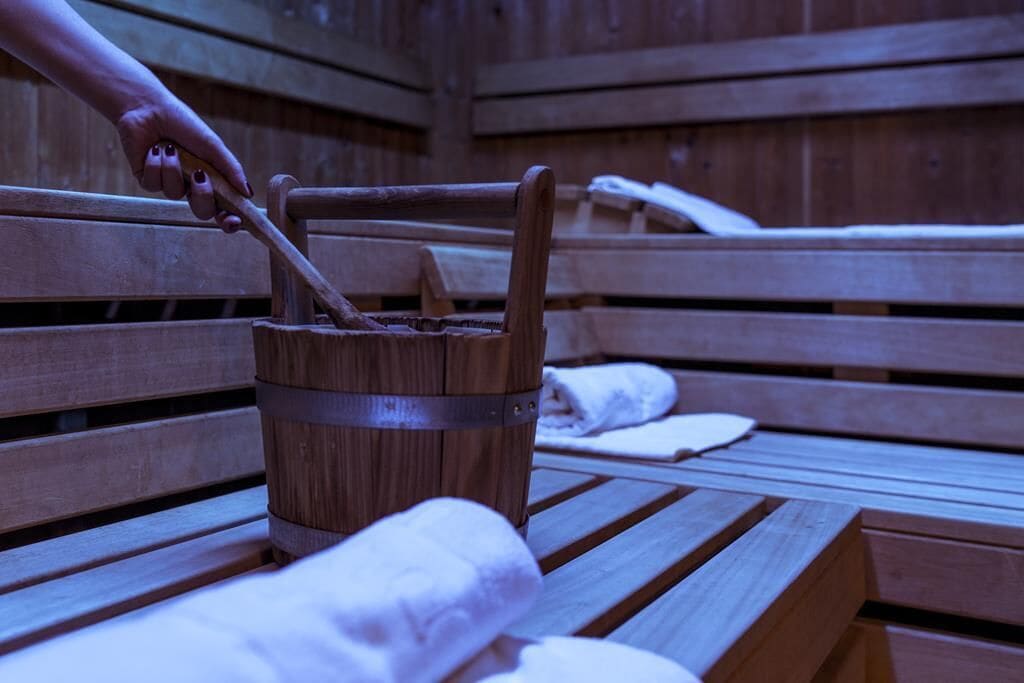Um banco de sauna de madeira com um balde de madeira e uma concha.