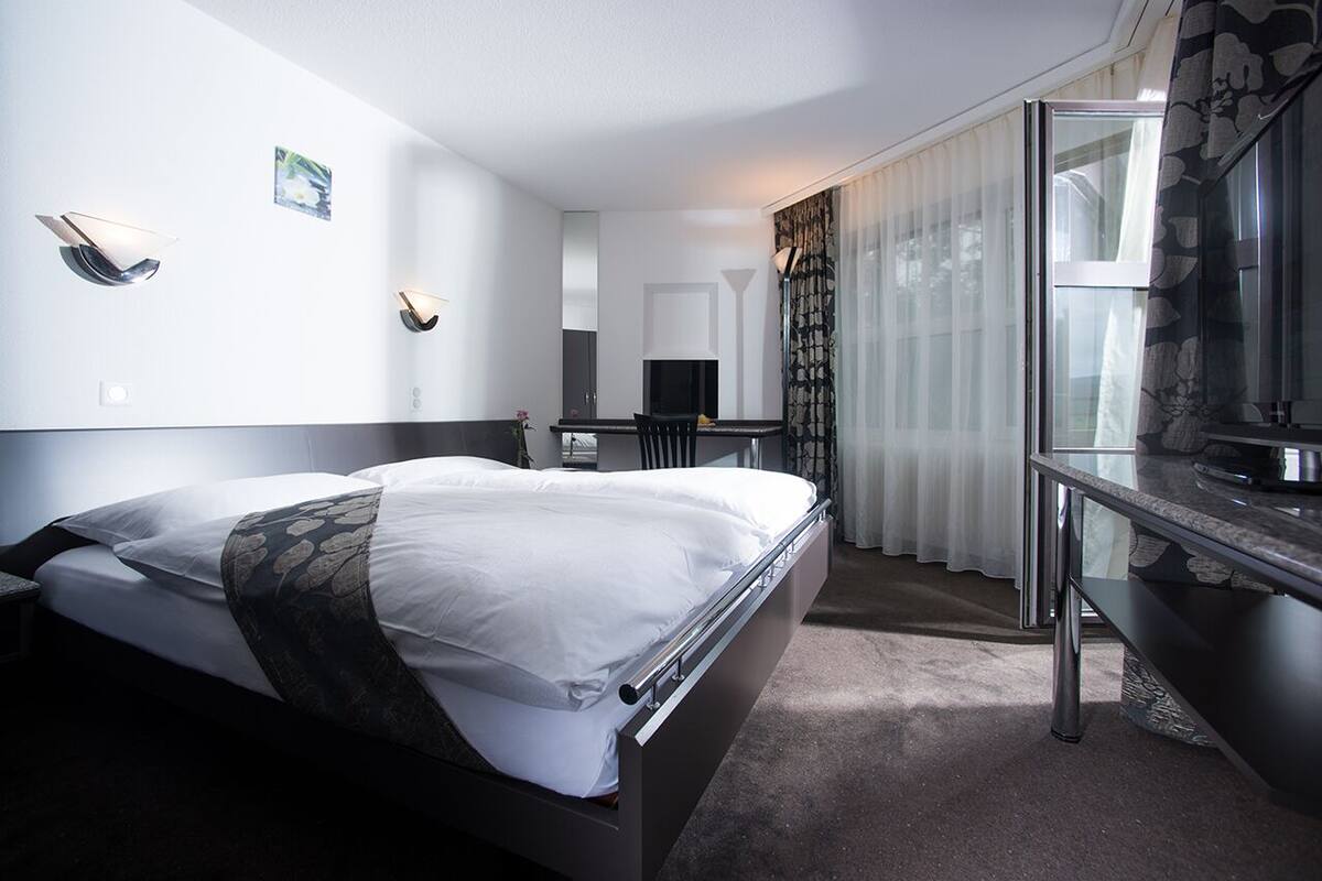 Quarto de hotel com uma cama, uma escrivaninha e uma cadeira.